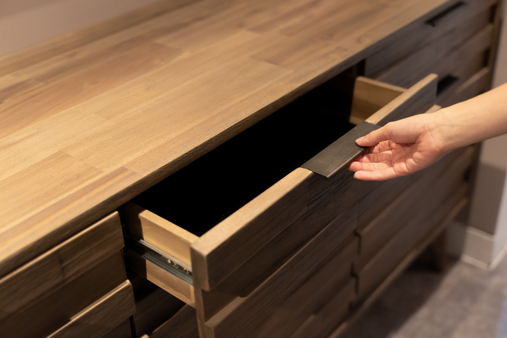 Hand opening a wooden drawer of a dresser with a minimalist modern design